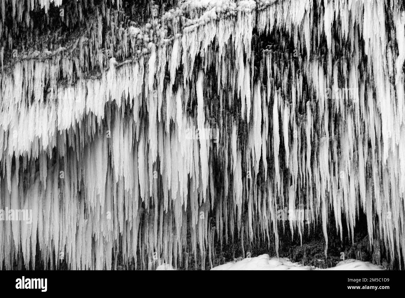 Icicles on the rock face at Skogafoss waterfall, black and white photo ...