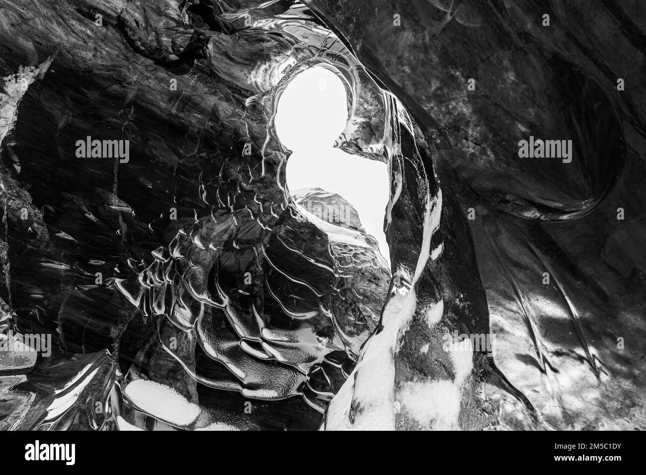 Ice cave open to the top with snow-covered ice combs, black and white ...