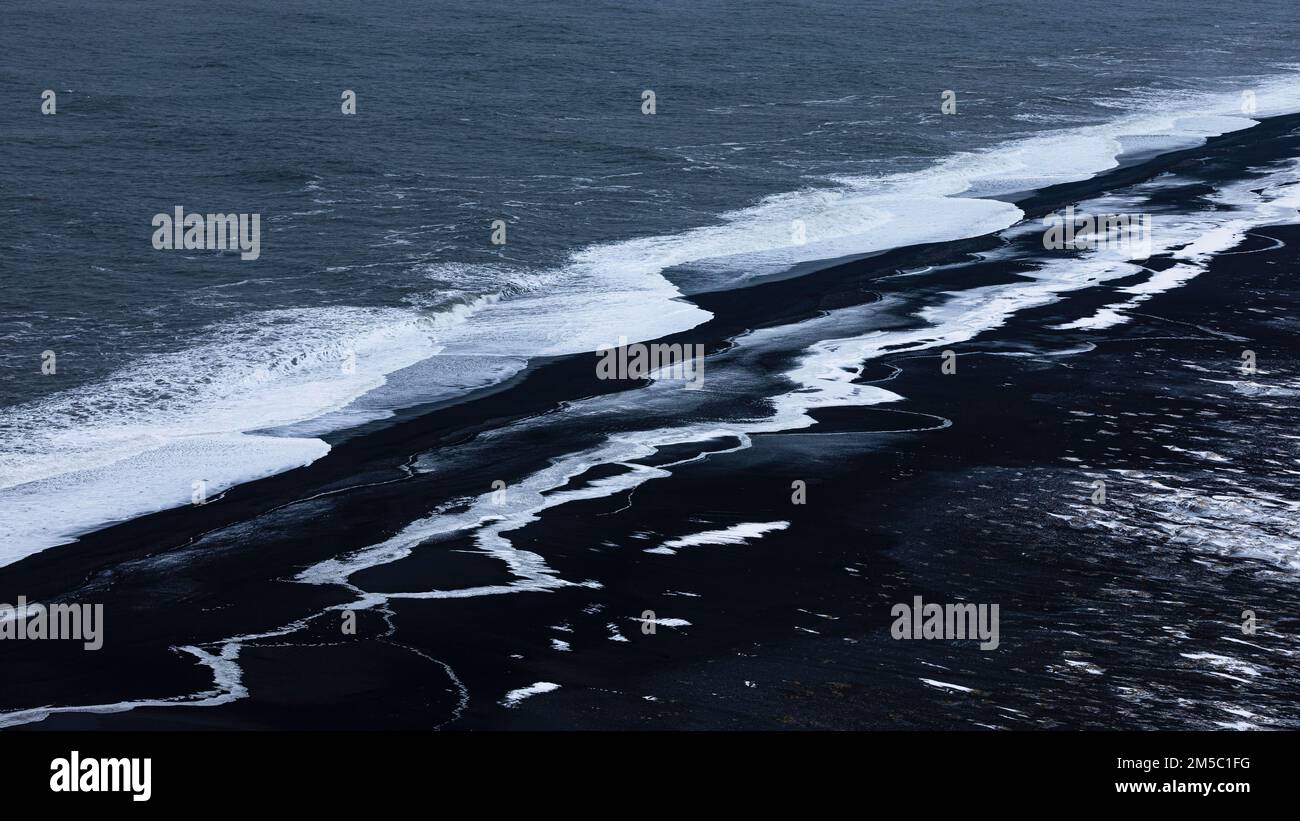 Foamy white waves and icy surfaces on the black pebble beach ...
