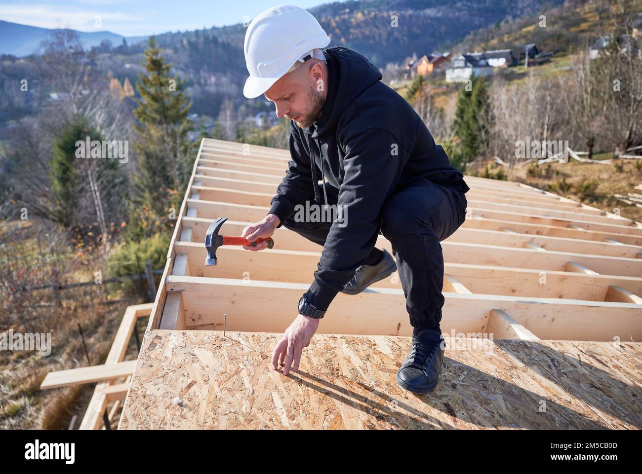 Carpenter hammering nail into OSB panel on the roof top of future ...