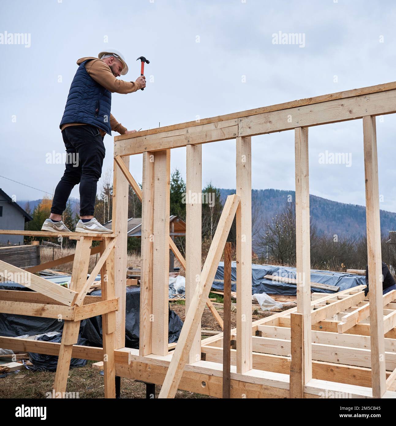Man worker building wooden frame house on pile foundation. Carpenter ...