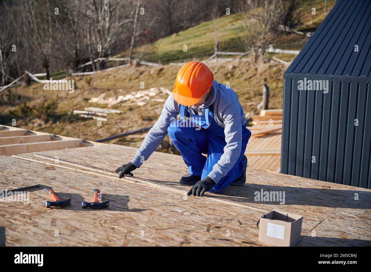 Man worker building wooden frame house. Carpenter measuring OSB sheet on rooftop. Carpentry ...