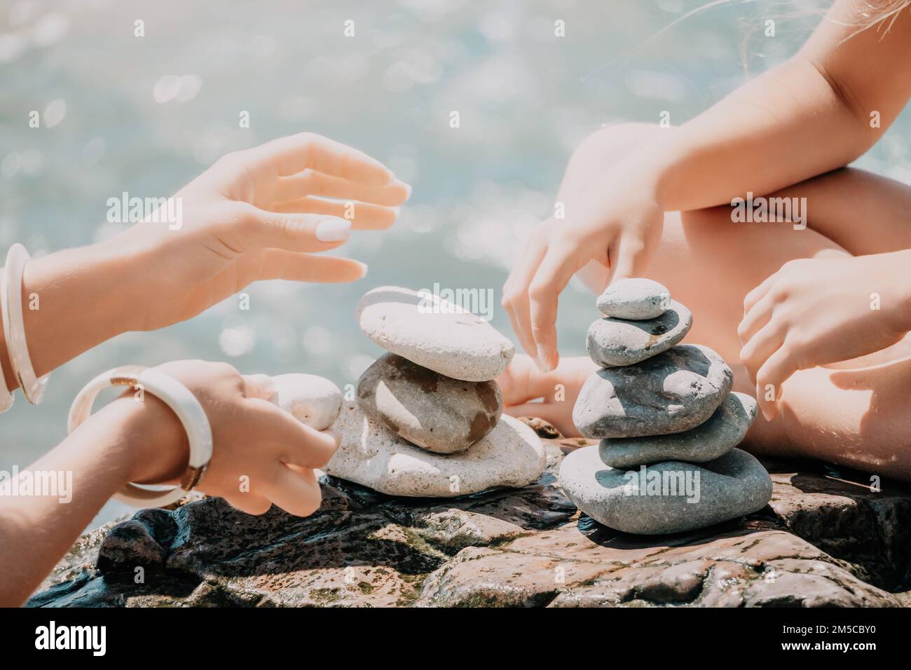 Woman with daughter bilds stones pyramid on seashore on a sunny day on ...