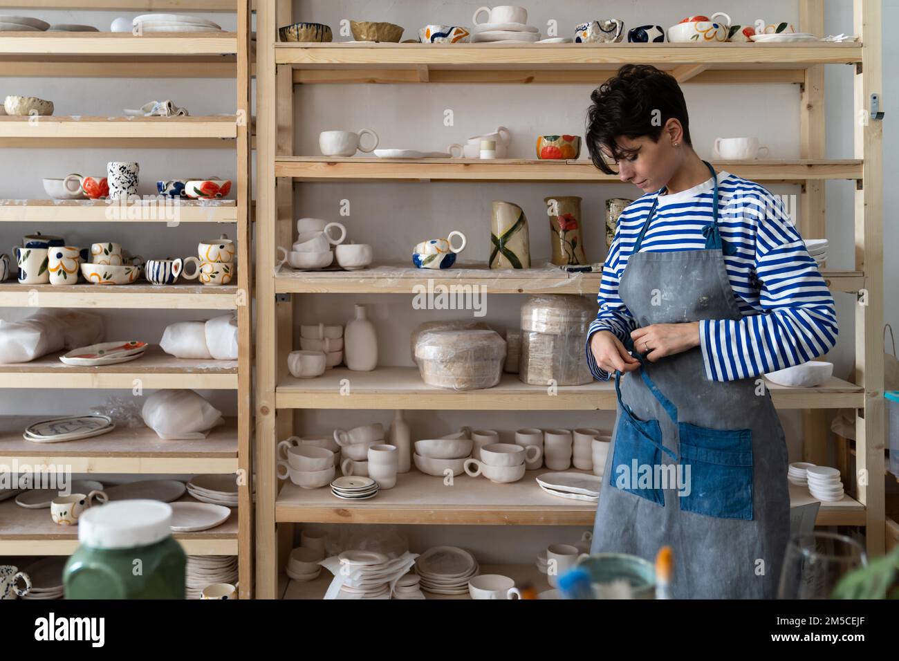 Creative artisan crafts woman tying apron and preparing for pottery ...