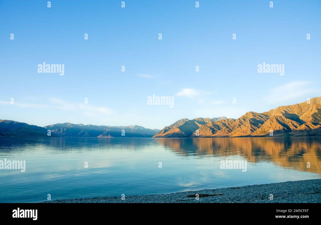 Peaceful Lake Wanaka in morning light surrounding hills and blue sky ...