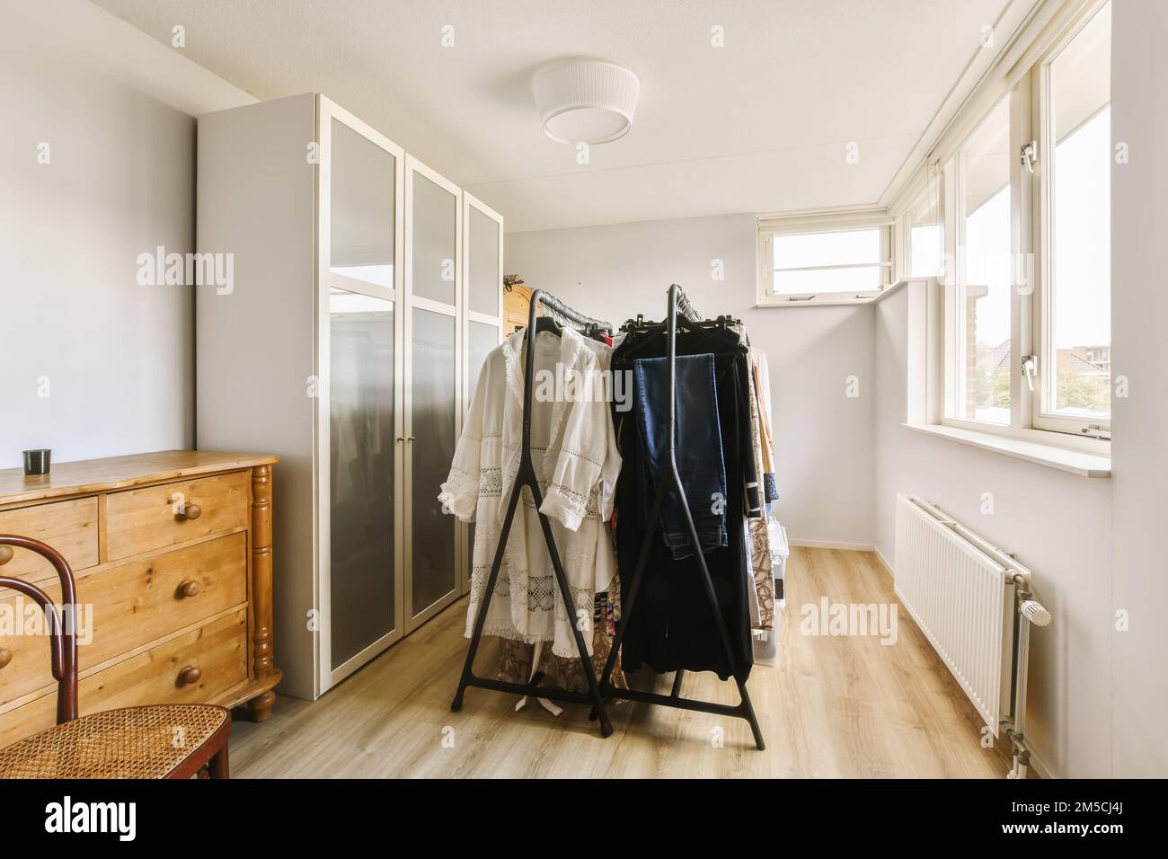 a room with clothes hanging on hangers and a chair in the corner, next ...