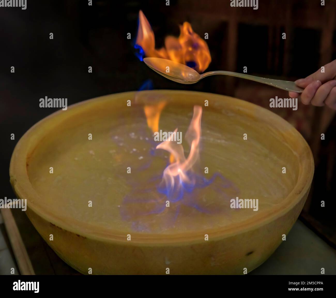 Flambe of Italian brandy lit on fire in pecorino wheel to soften the ...