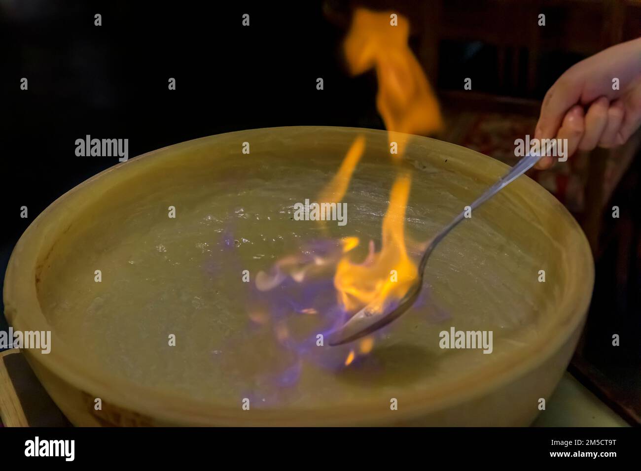 Flambe of Italian brandy lit on fire in pecorino wheel to soften the ...