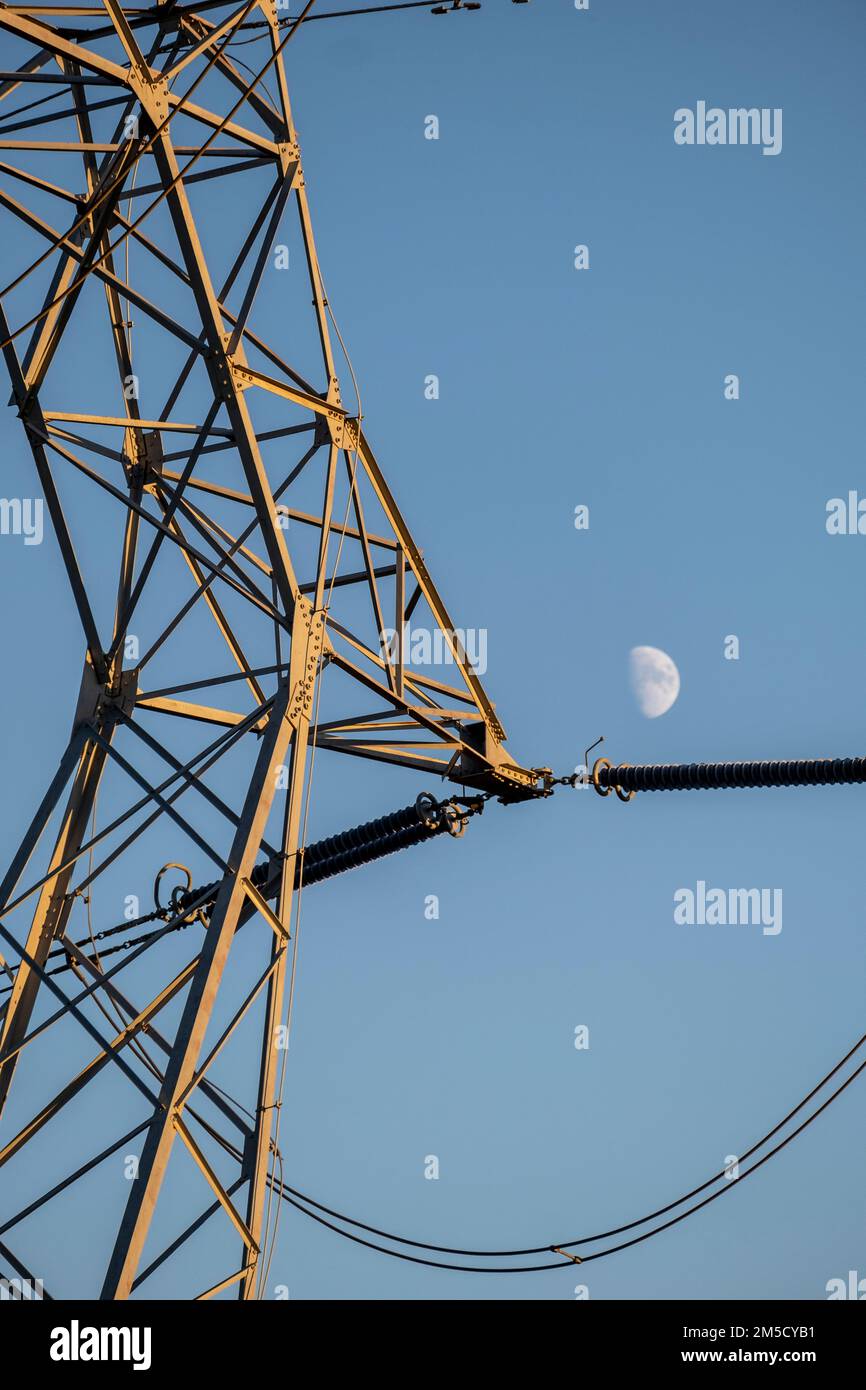 A vertical low angle of a high-voltage cable tower against half moon in ...