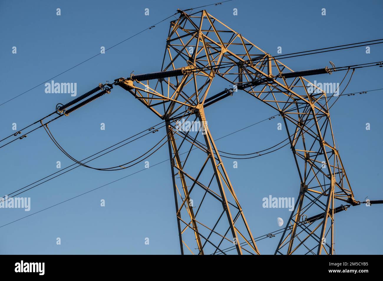 A low angle of a high-voltage cable tower against half moon in the blue ...