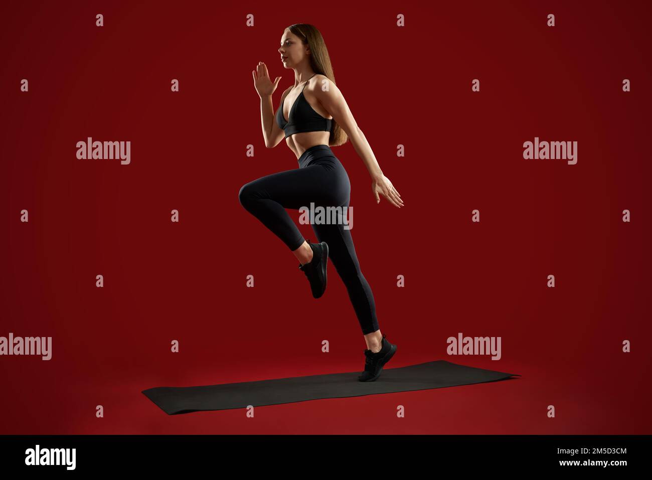 Brunette jumper woman highly jumping on one leg in red studio, training ...