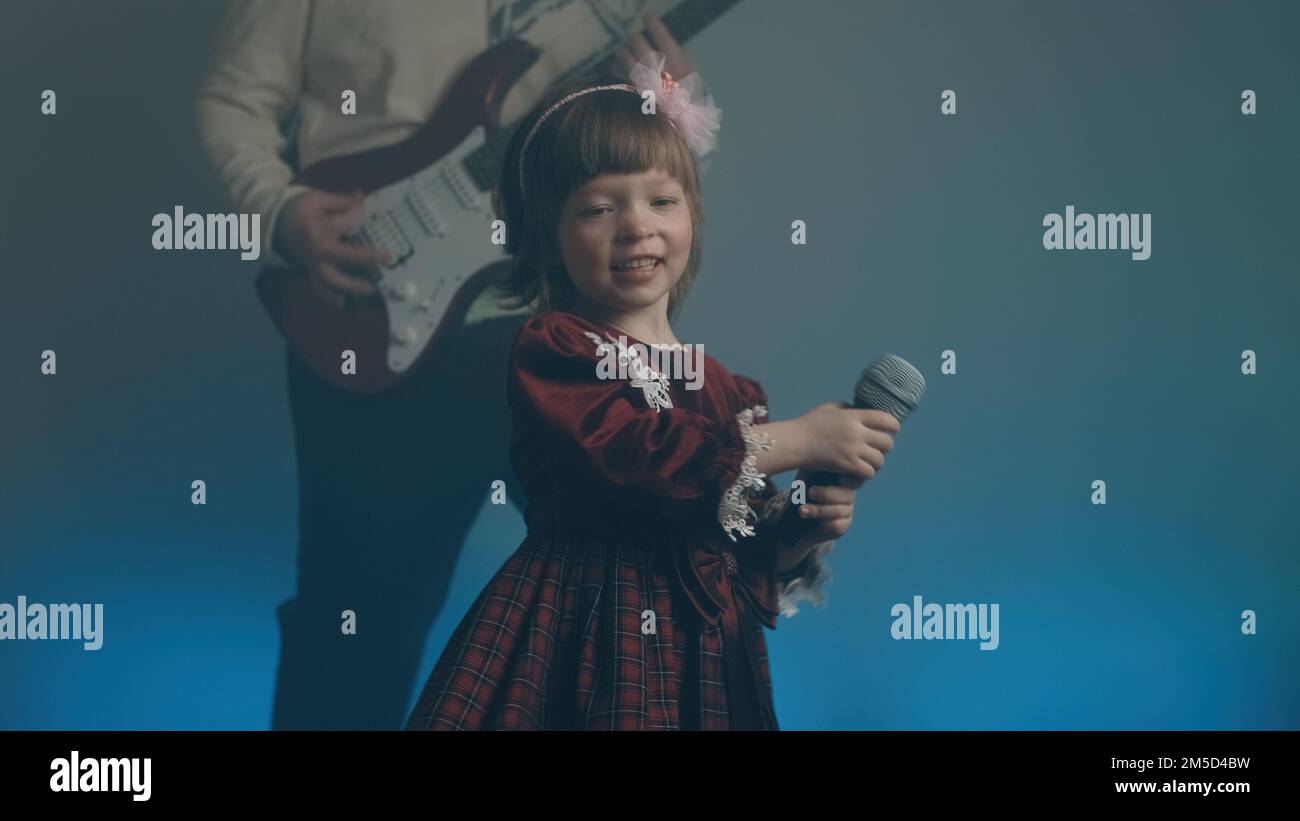 Little girl in vintage dress sings on stage, her father plays an ...