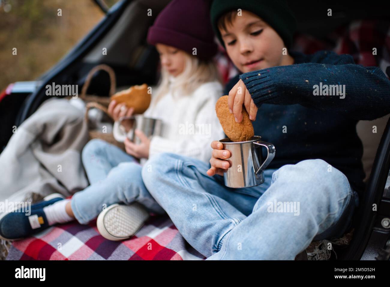 Two children eating biscuits and drinking tea sitting in car body ...