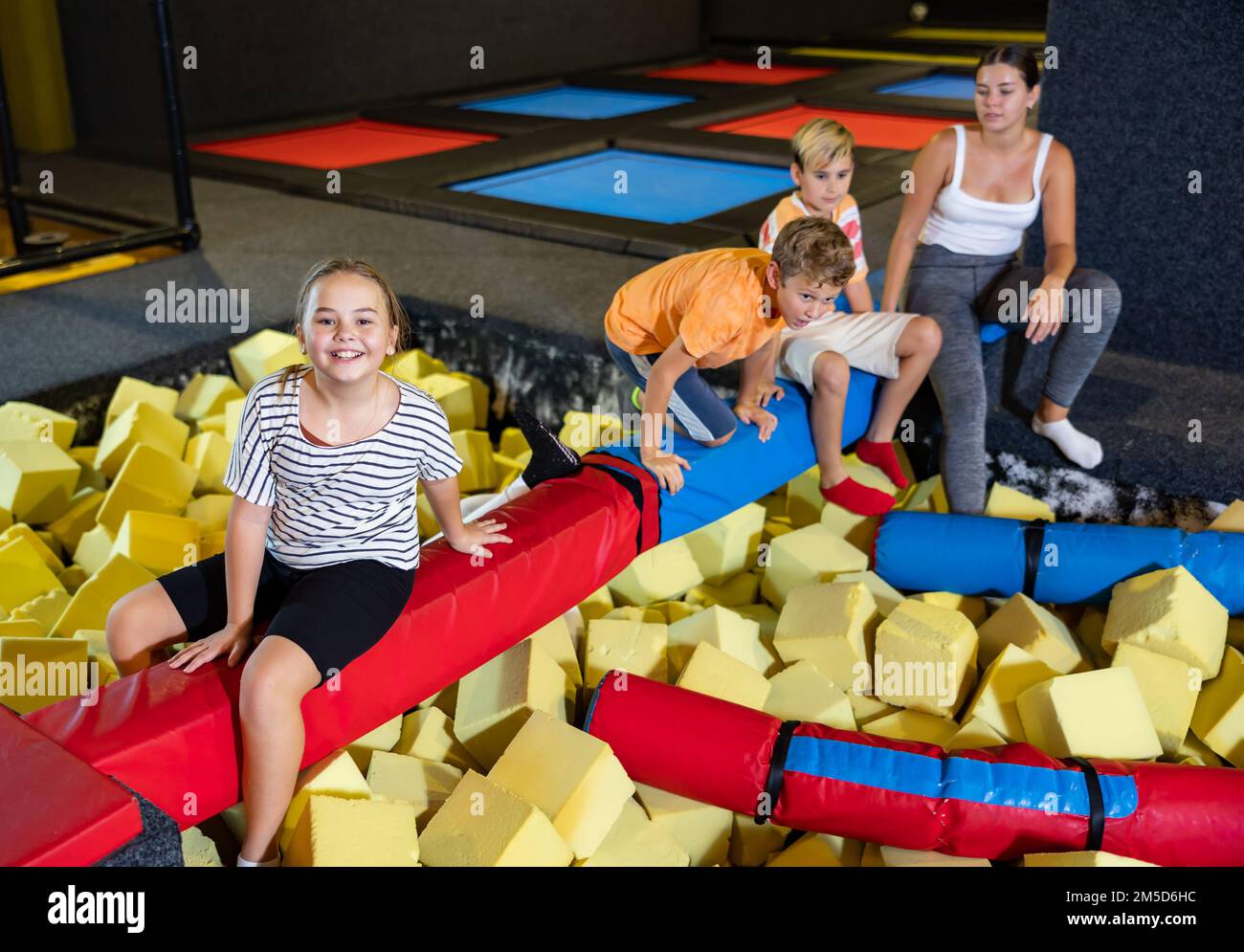 Happy tween children with woman sitting on soft beam above foam pit ...