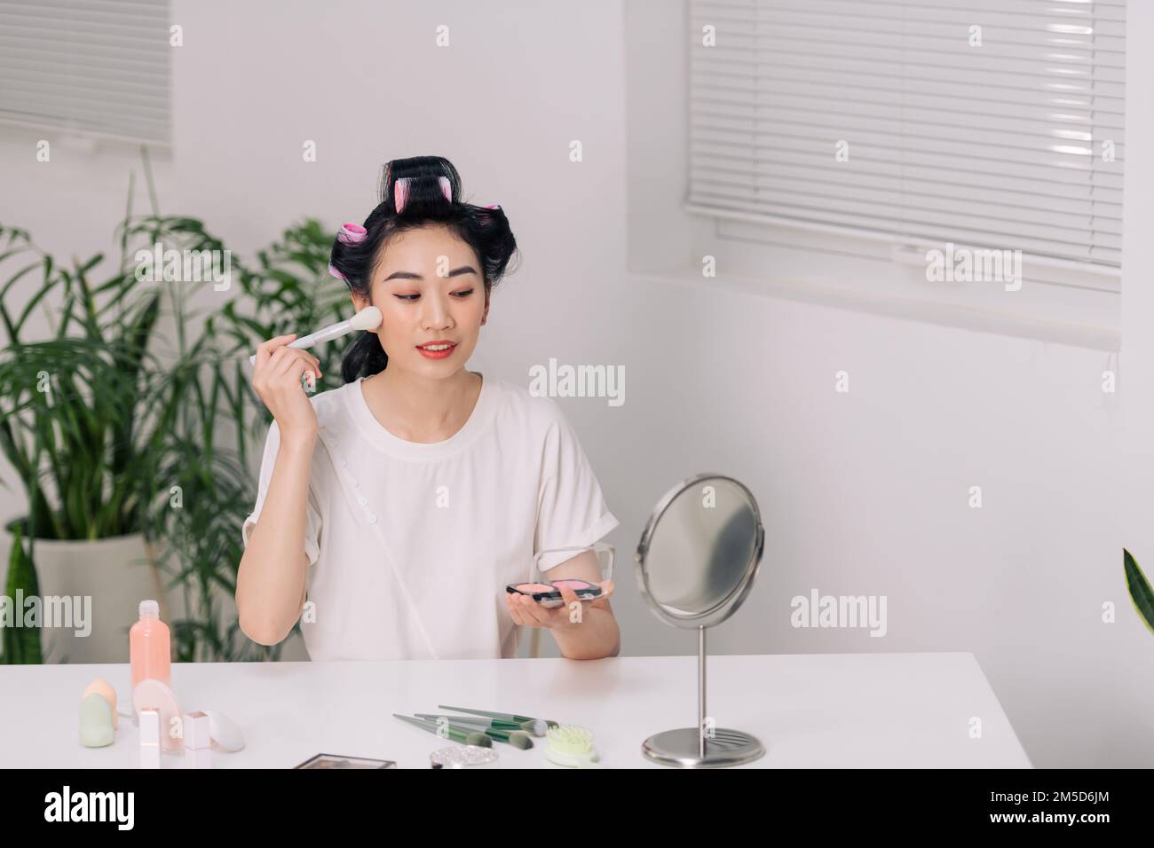 Beautiful young woman makes blush on her face using makeup brush while ...