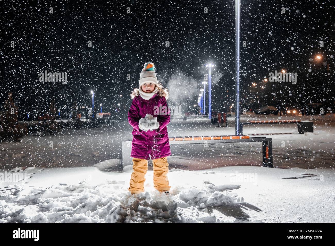 A little girl is very happy with the first snow on a cold winter night ...
