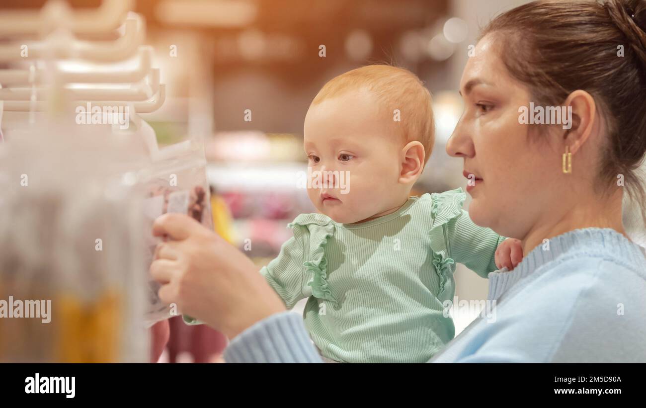 Baby girl with serious expression helps mother choose outfit for home ...