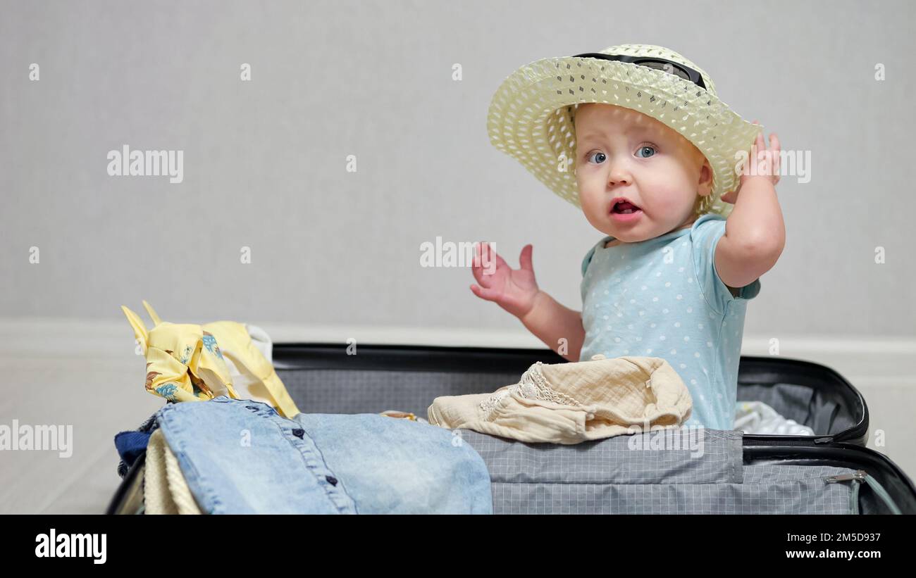 Excited baby girl sits in suitcase and takes off straw hat Stock Photo ...