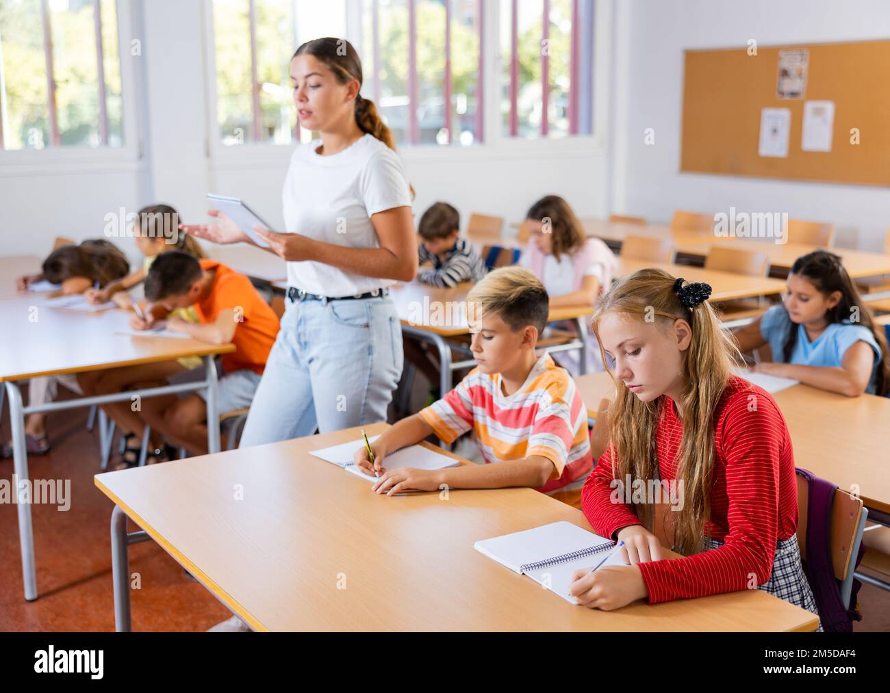School kids with pens and notebooks studying in classroom with teacher ...