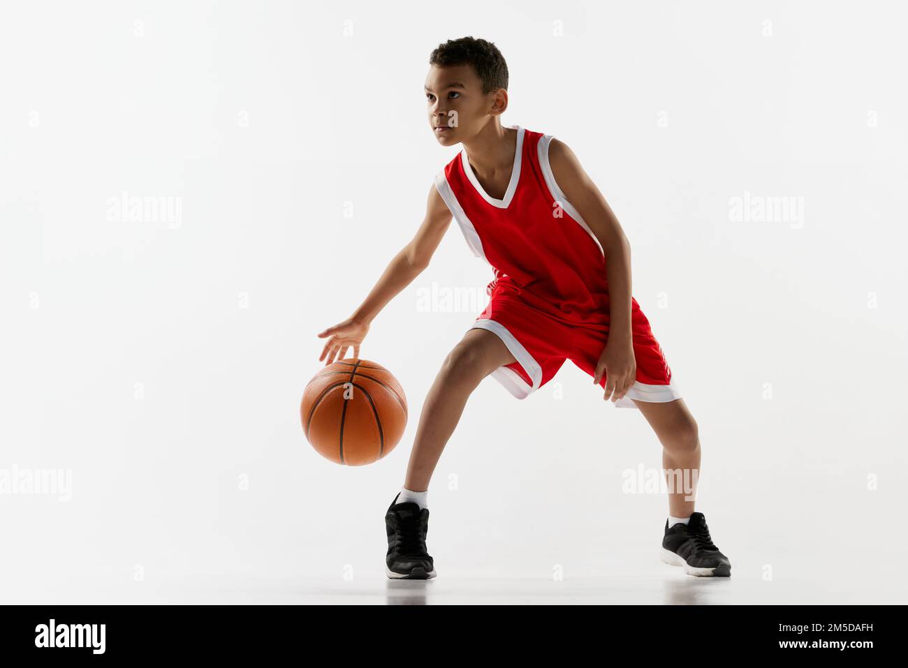 Portrait of boy in red uniform training, playing basketball, dribbling ...