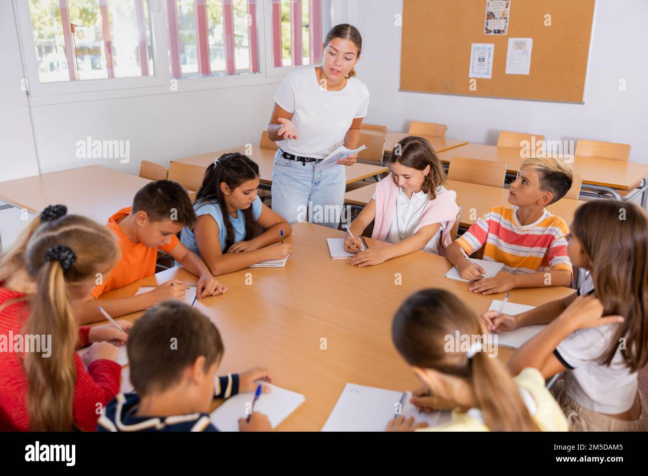 Female teacher conducting lesson with preteen children sitting around ...