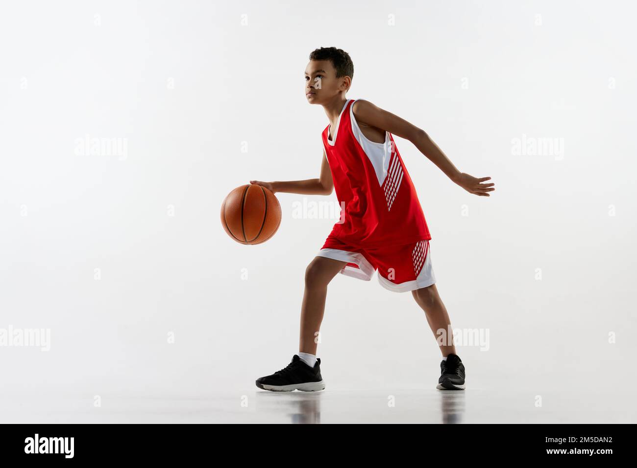 Portrait of boy in red uniform training, playing basketball, dribbling ...