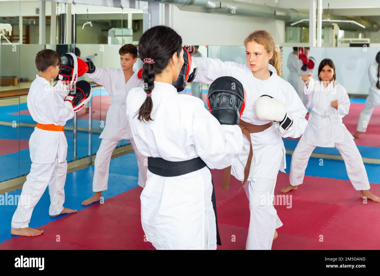 Female trainer in boxing gloves conducts sparring and teaches punches to girl in karate and self ...