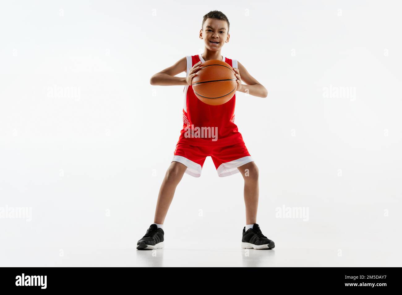 Portrait of boy in red uniform training, playing basketball over grey ...