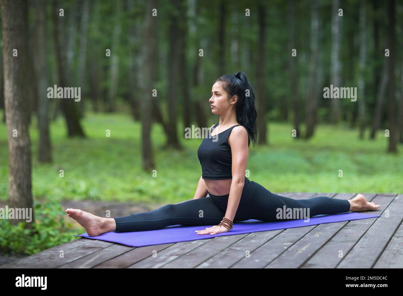 A young sports woman practicing yoga, doing a hanumanasana exercise ...