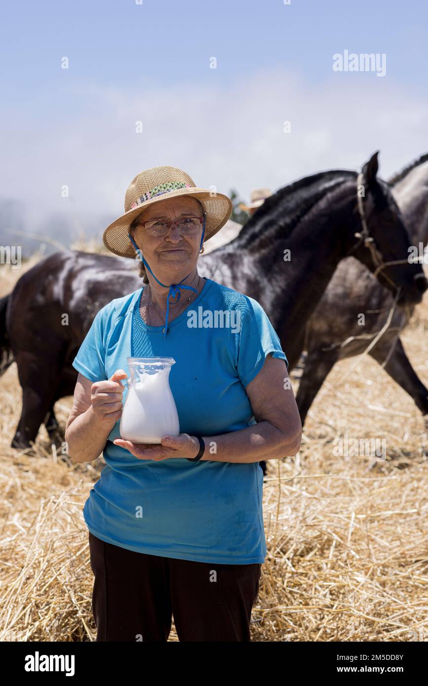 Woman holds a jug of goat milk at the threshing day, Dia de la trilla ...