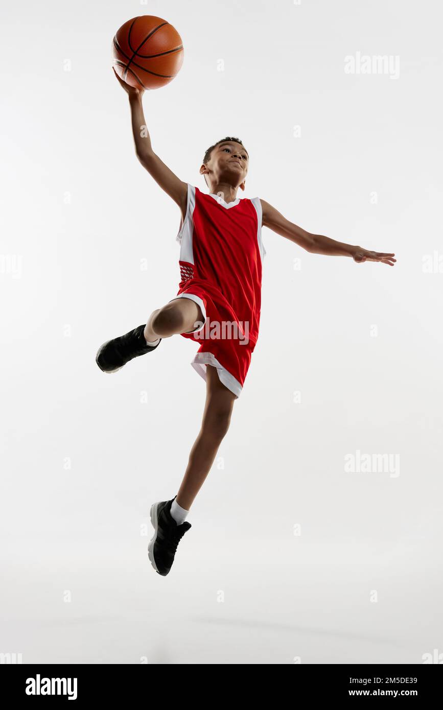 Portrait of boy in red uniform training, playing basketball, throwing ...