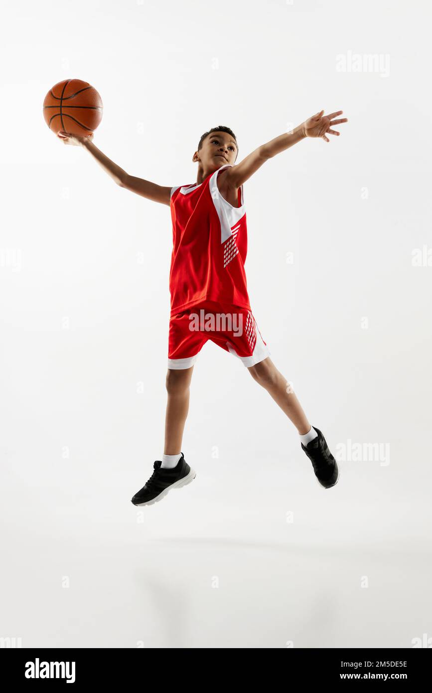Portrait of boy in red uniform training, playing basketball, throwing ...