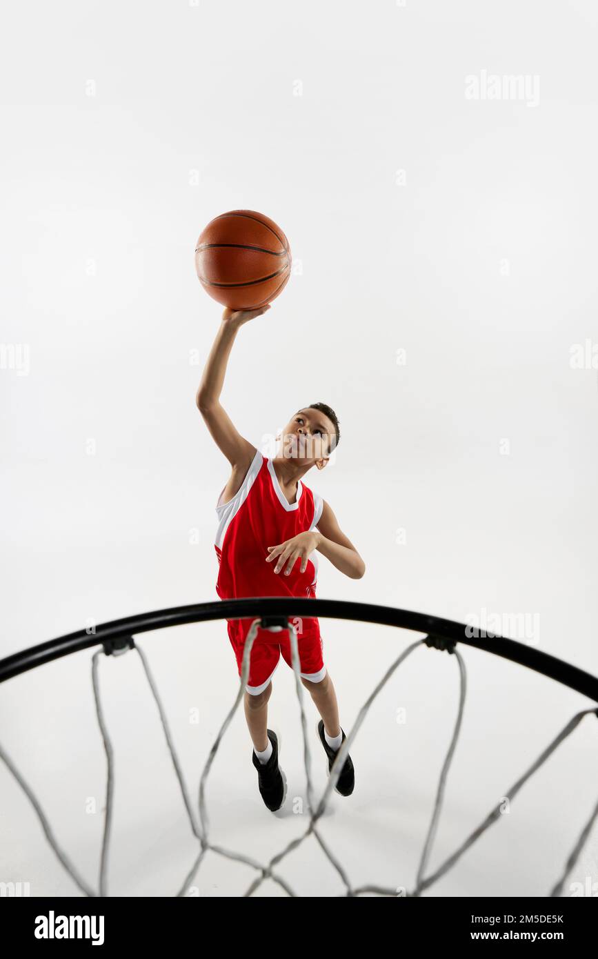 Portrait of boy in red uniform training, playing basketball, throwing ...