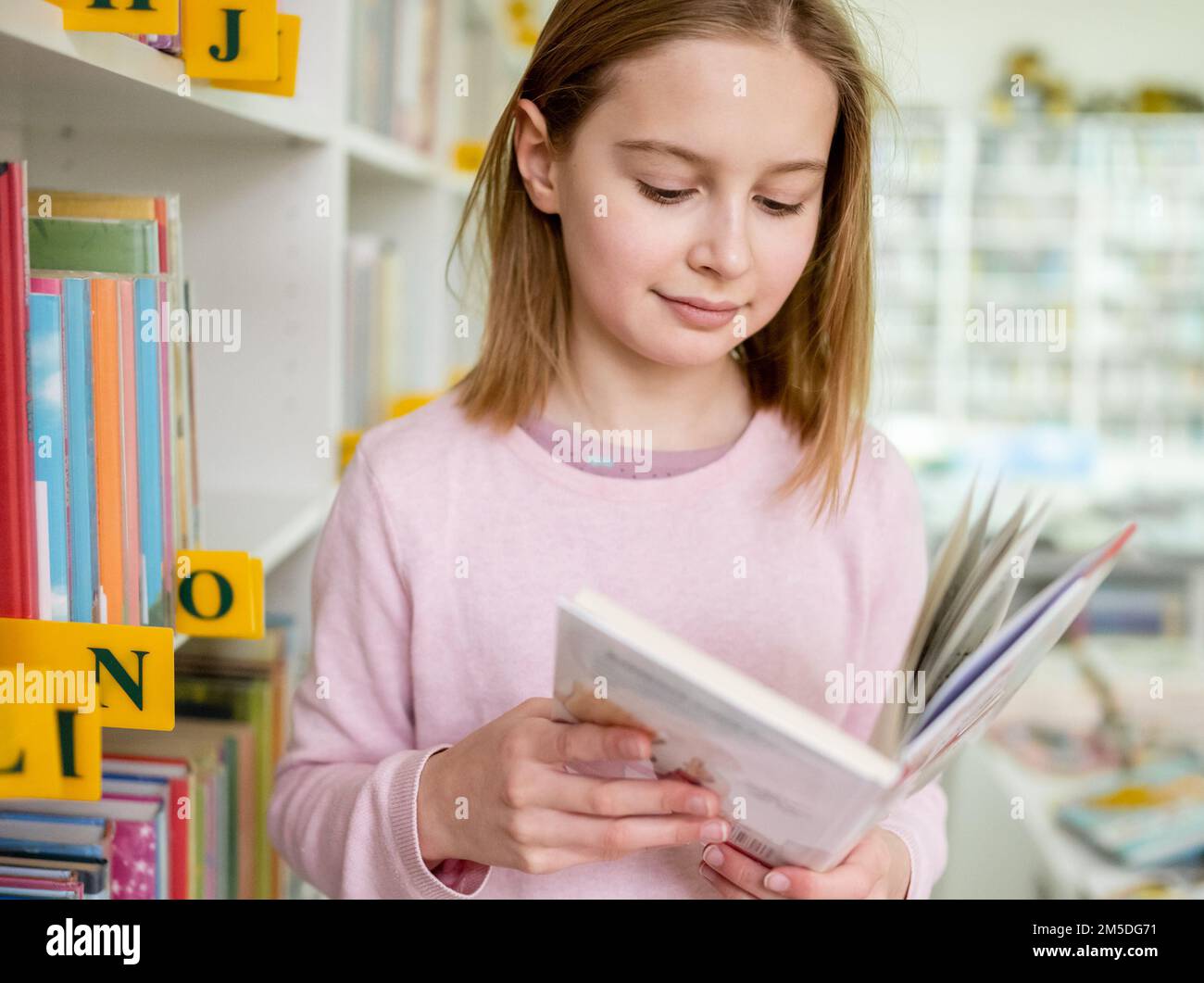 Pretty girl child reading book in library Stock Photo - Alamy