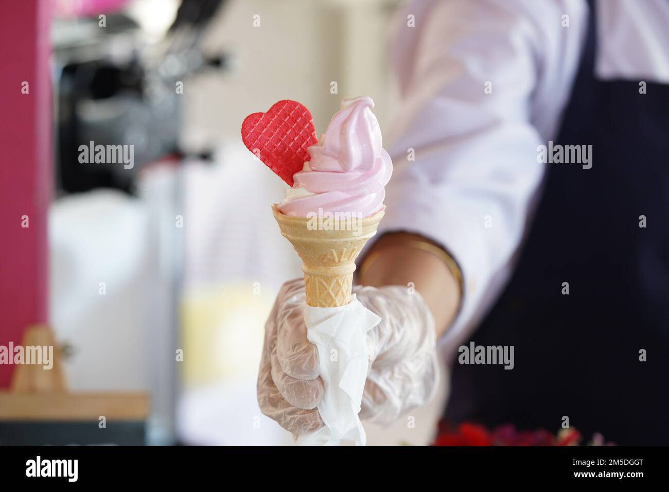 A worker with gloves holding an ice cream cone with a mix flavours pink ...