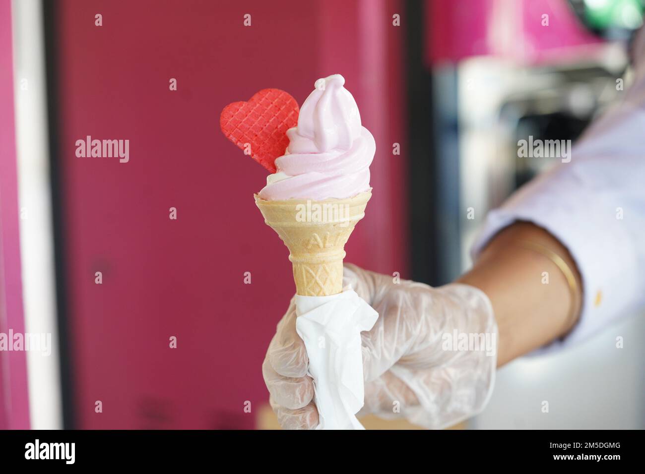 A worker with gloves holding an ice cream cone with a mix flavours pink ...