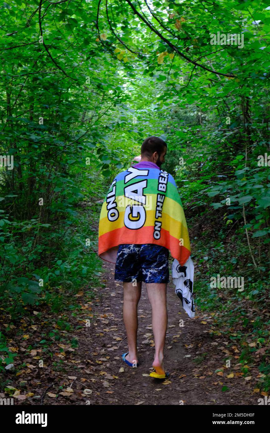 A male with LGBT flag on his shoulders walking on a park path with ...