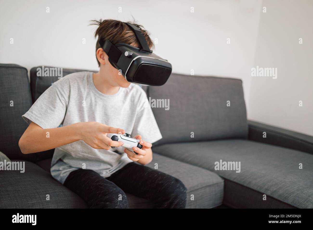Caucasian male child wearing a VR headset and holding a gamepad while ...