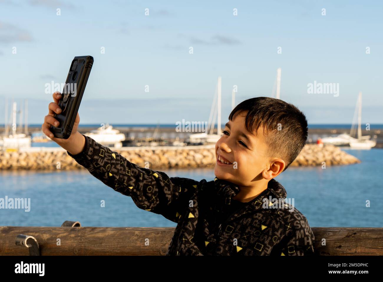Happy boy in casual clothes smiling and taking selfie against sea with ...
