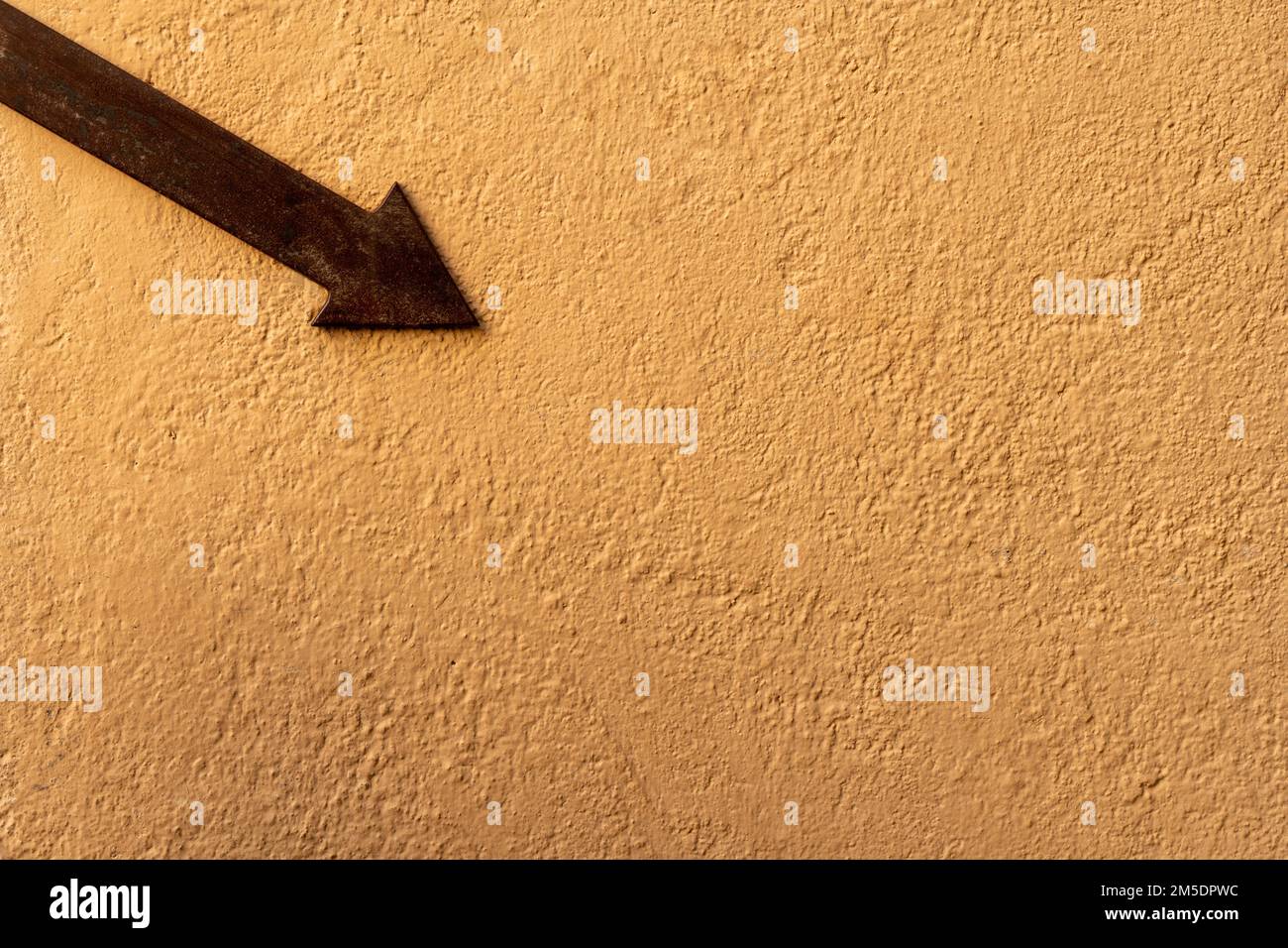 Black arrow pointing down on ocher stucco wall of building on city ...