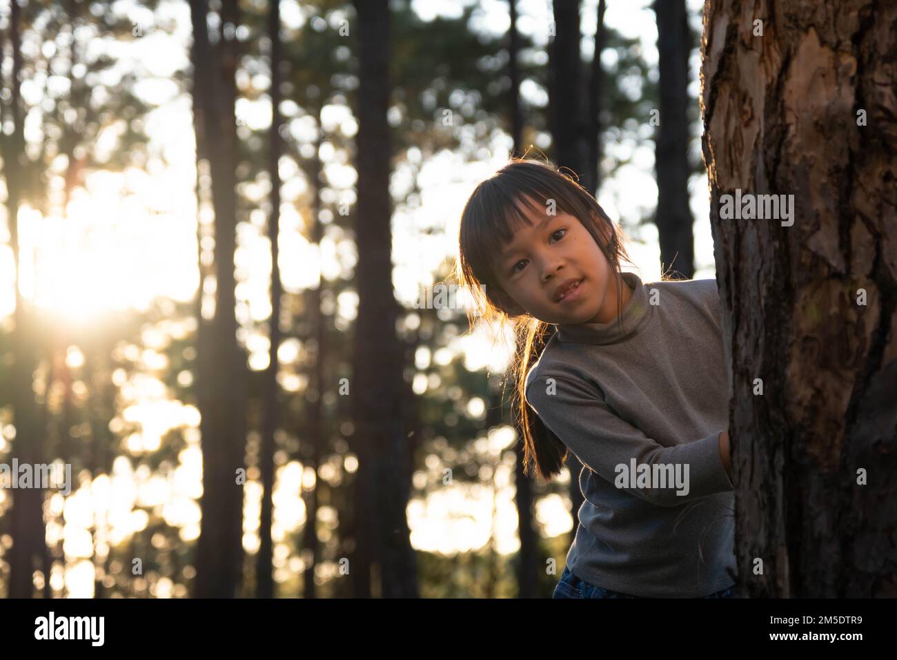 Funny little girl peeking out from behind tree in winter park. Cute ...