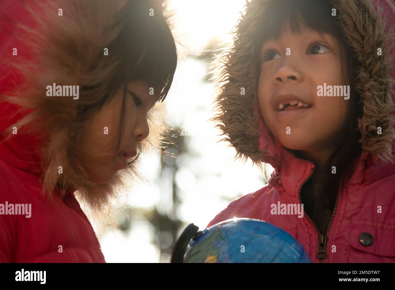 Two cute Asian girls learning a model of the world on nature background ...