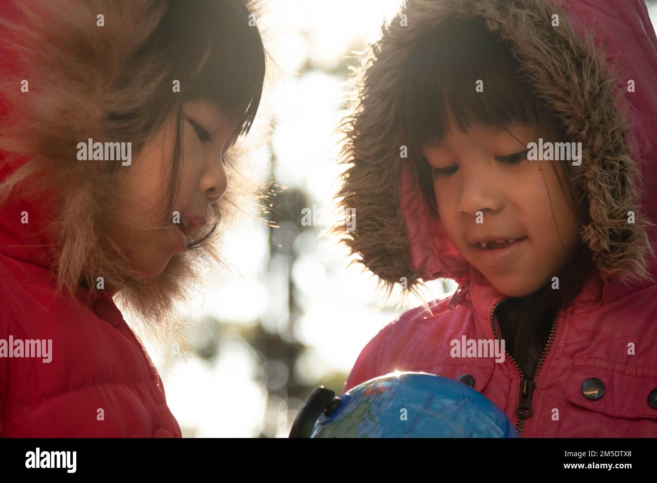 Two cute Asian girls learning a model of the world on nature background ...