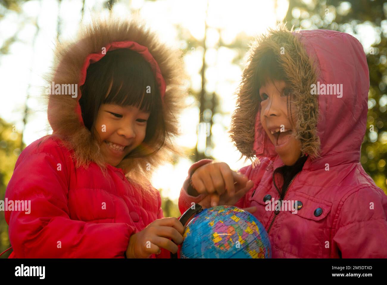 Two cute Asian girls learning a model of the world on nature background ...