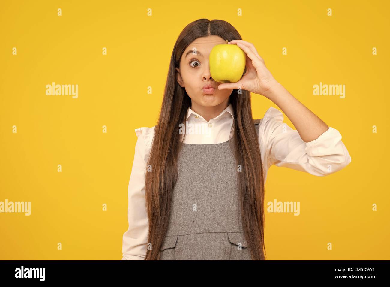 Funny face. Child girl eating an apple over isolated yellow background ...
