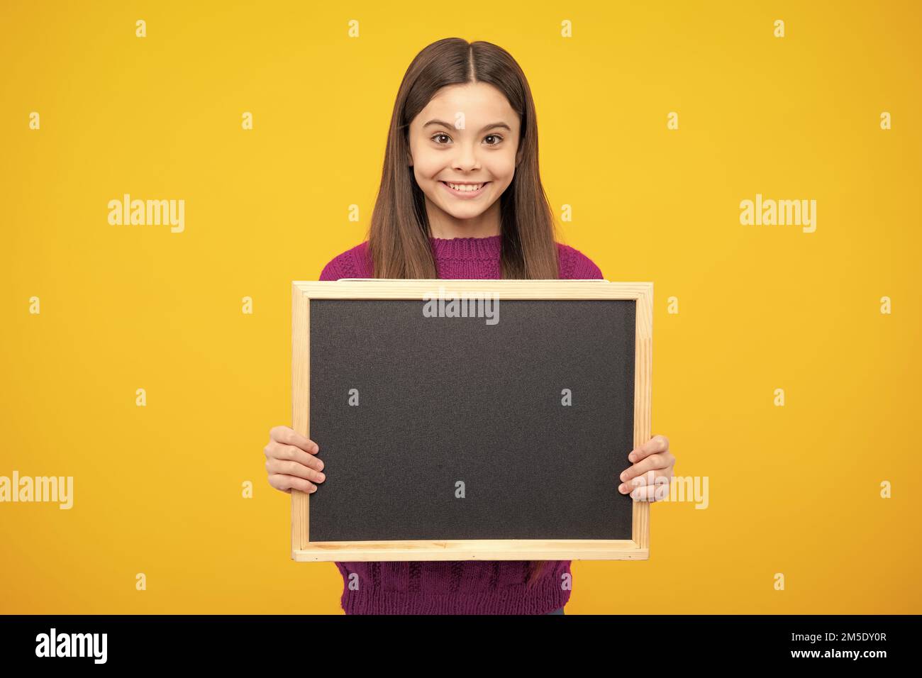 Teenage girl child holding blackboard, isolated on a yellow background ...
