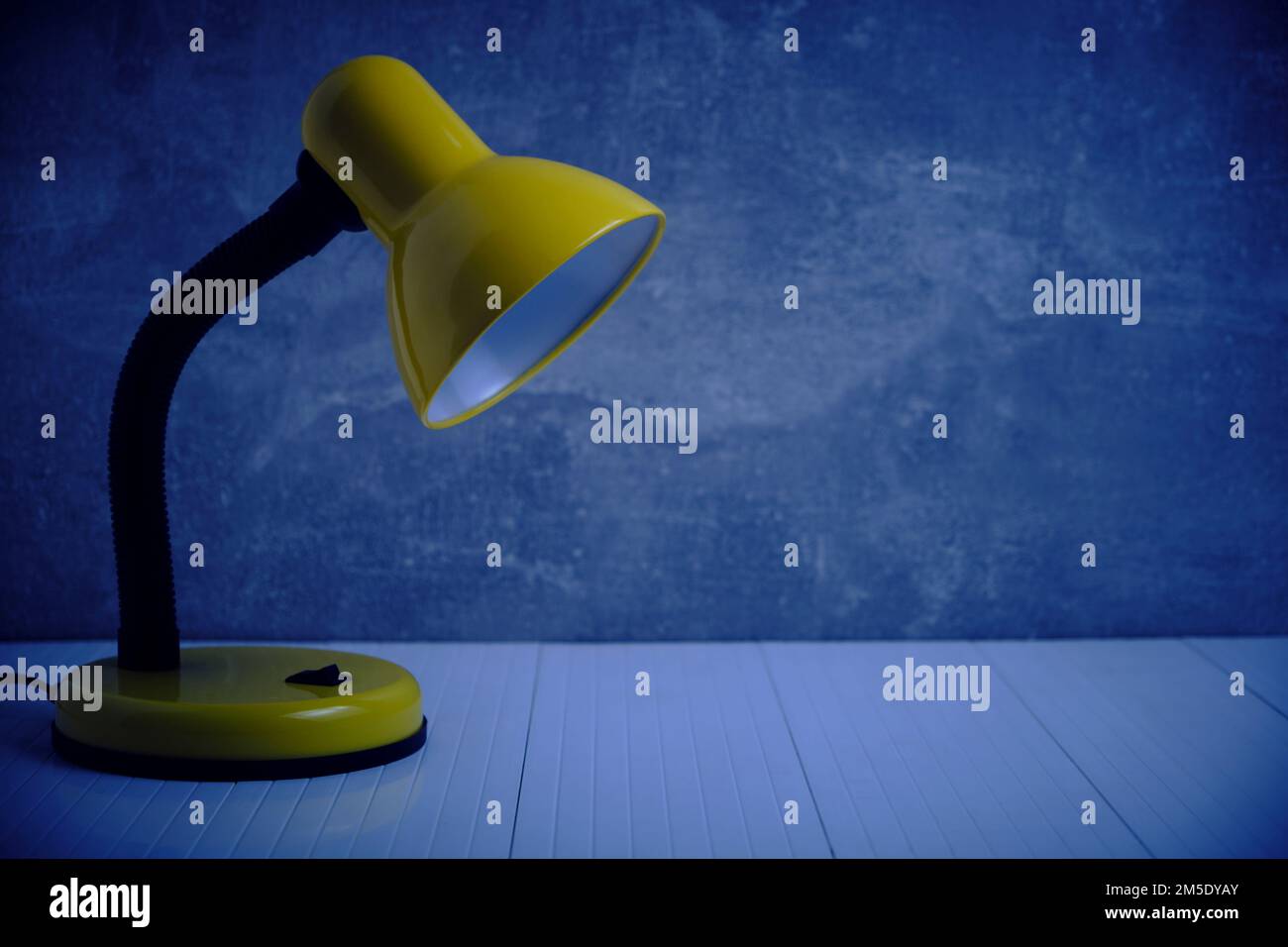 Bright yellow desk lamp, turned off, standing in dark against ...