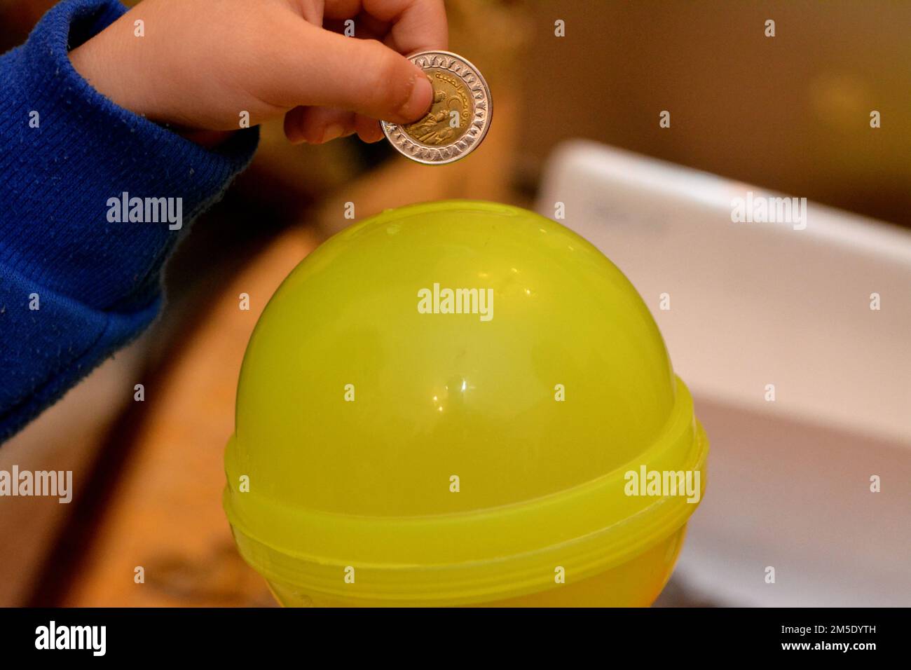 A young child putting a coin in a plastic child saving bank, concept of ...