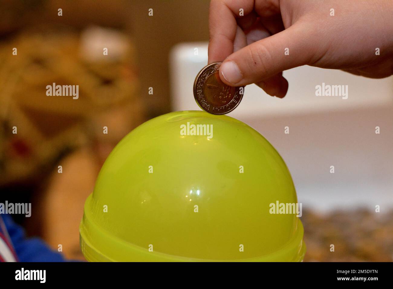 A young child putting a coin in a plastic child saving bank, concept of ...