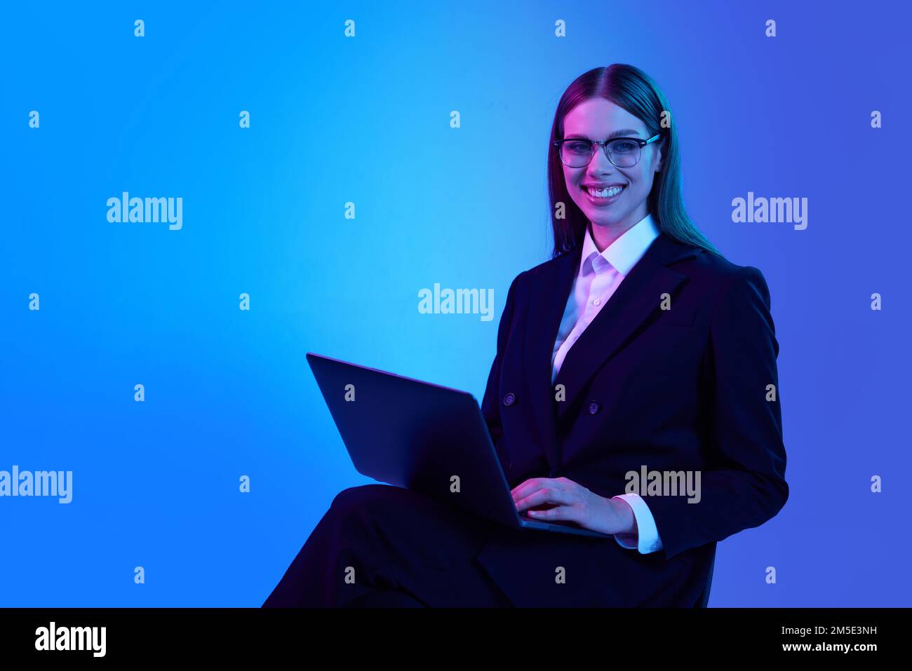 Woman in stylish official suit working on laptop over blue background ...
